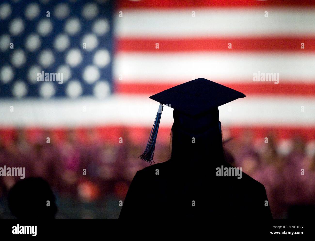 A graduating student walks down the aisle, waving back to his family ...