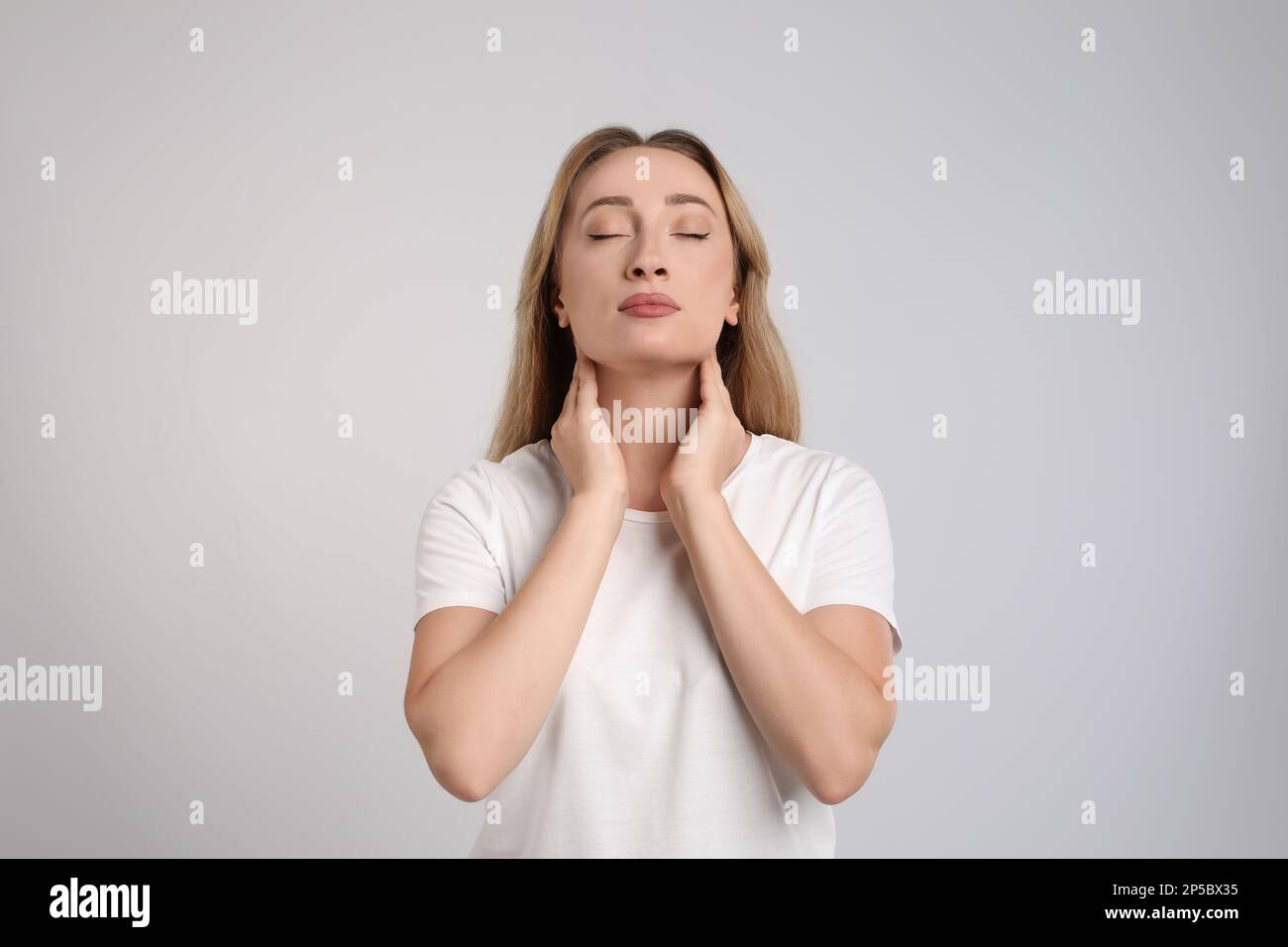 Young woman doing thyroid self examination on light grey background ...