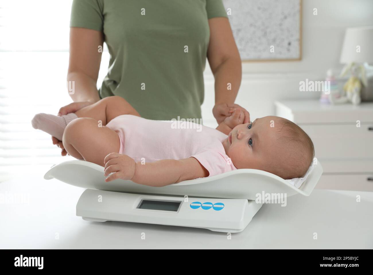 Young woman weighting her cute baby at home, closeup. Health care Stock ...