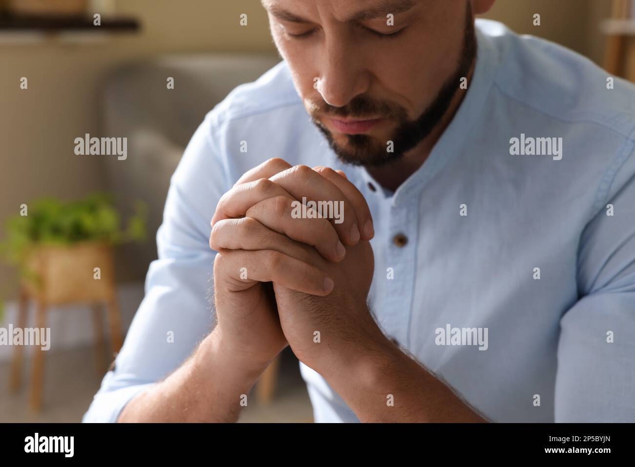 Religious man with clasped hands praying indoors, closeup Stock Photo ...