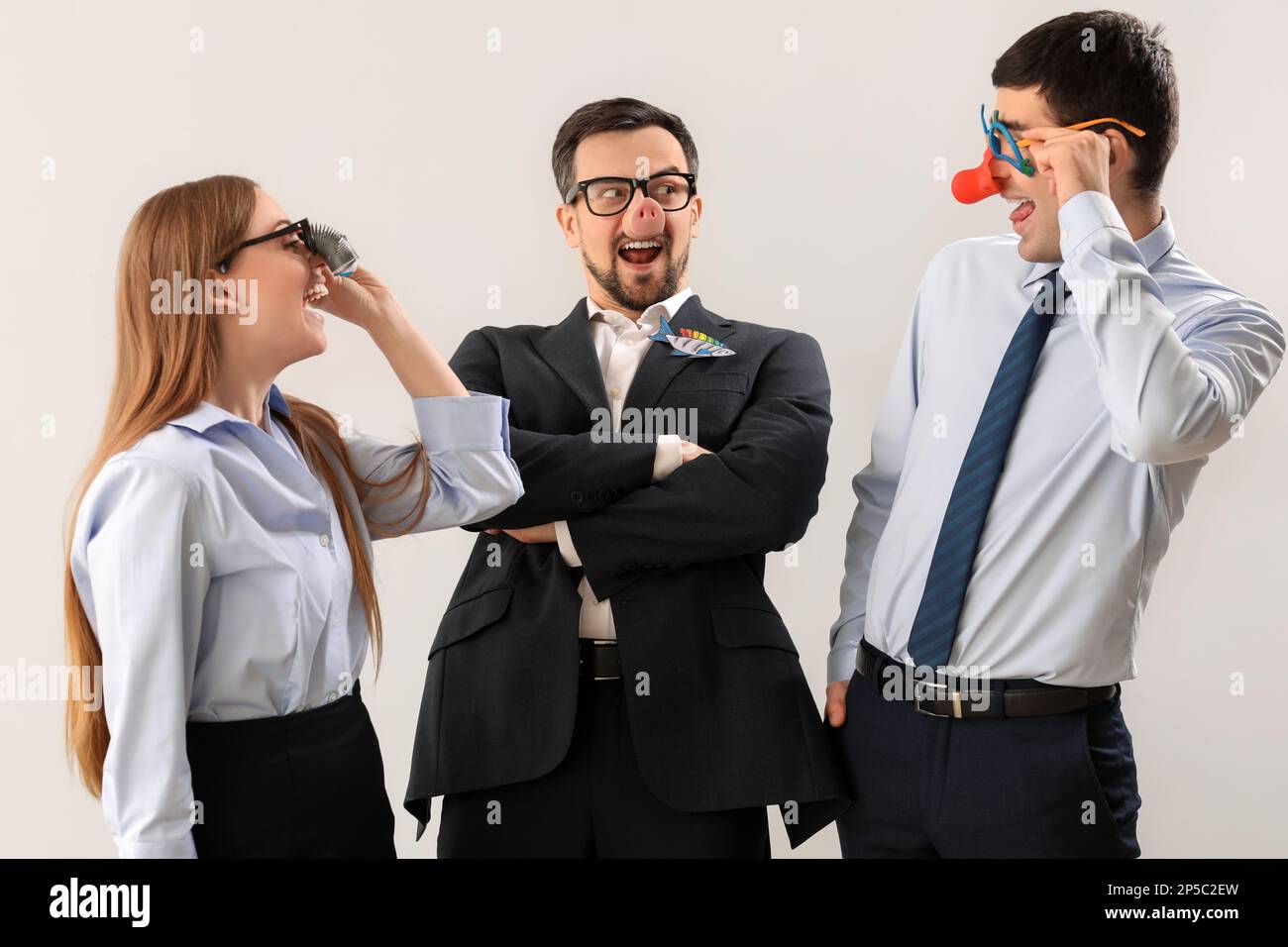 Business colleagues in funny disguise on light background. April Fools ...