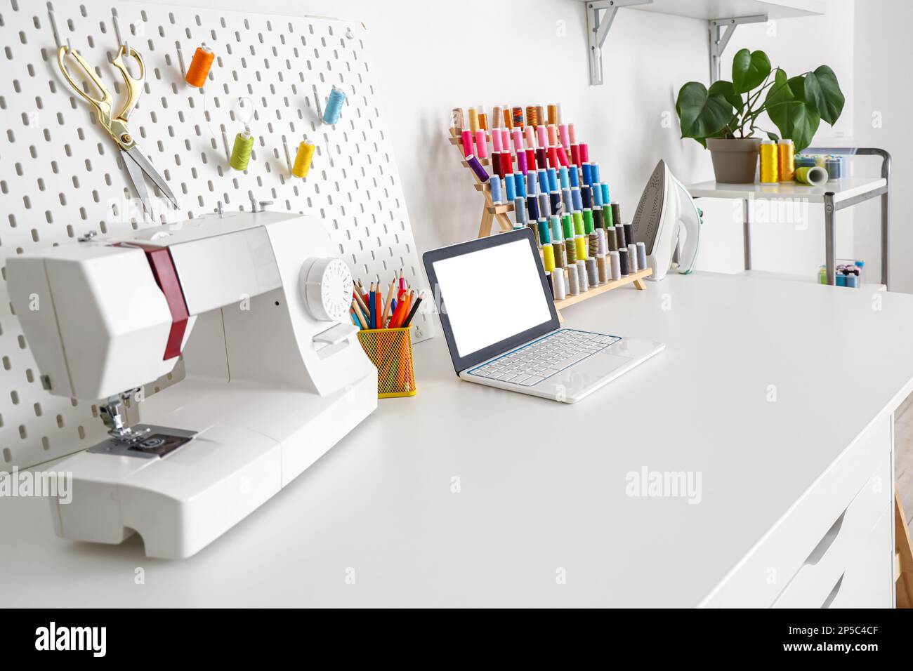 Tailor's workplace with laptop, sewing machine and thread spools in ...
