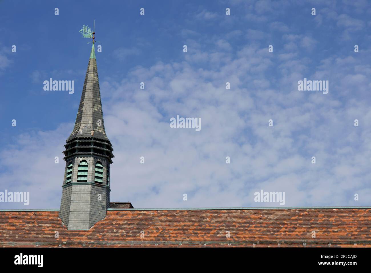 Tiled, red roof of historic building. Spire with weathervane of ship on ...