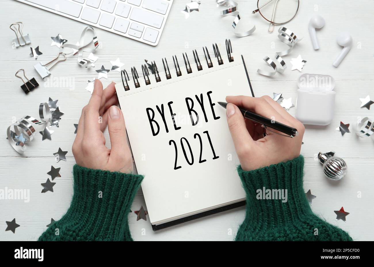 Woman writing phrase Bye Bye 2021 in notebook at white wooden table ...