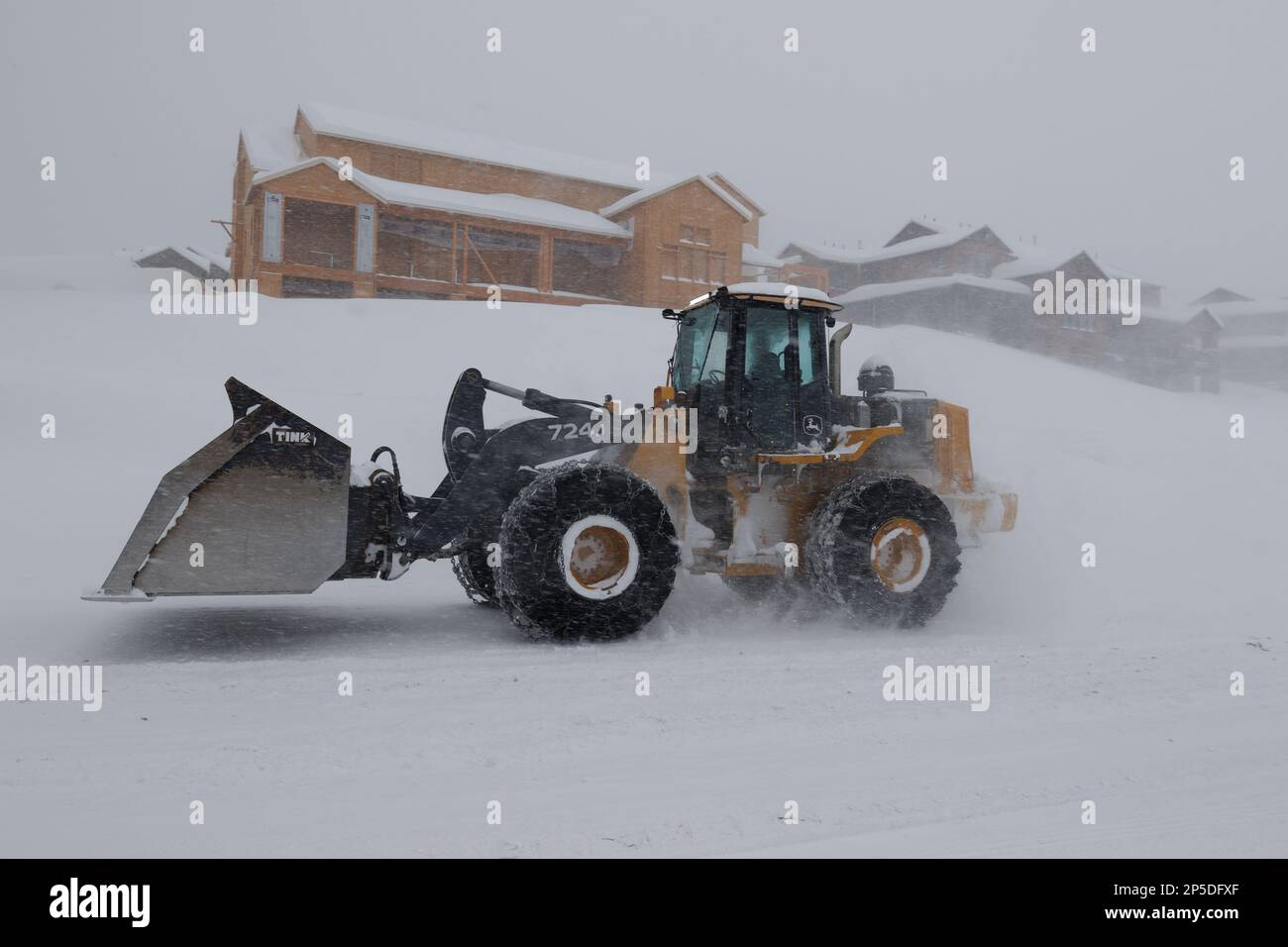 A yellow tractor with tire chains drives past a home under construction ...