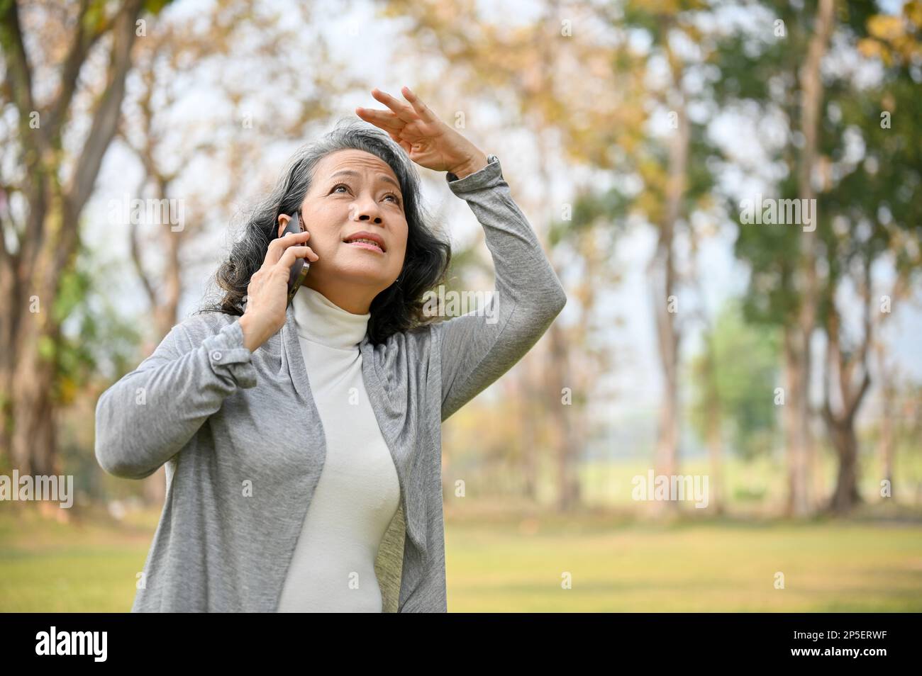 Tired 60s aged Asian woman talking on the phone, calling someone ...