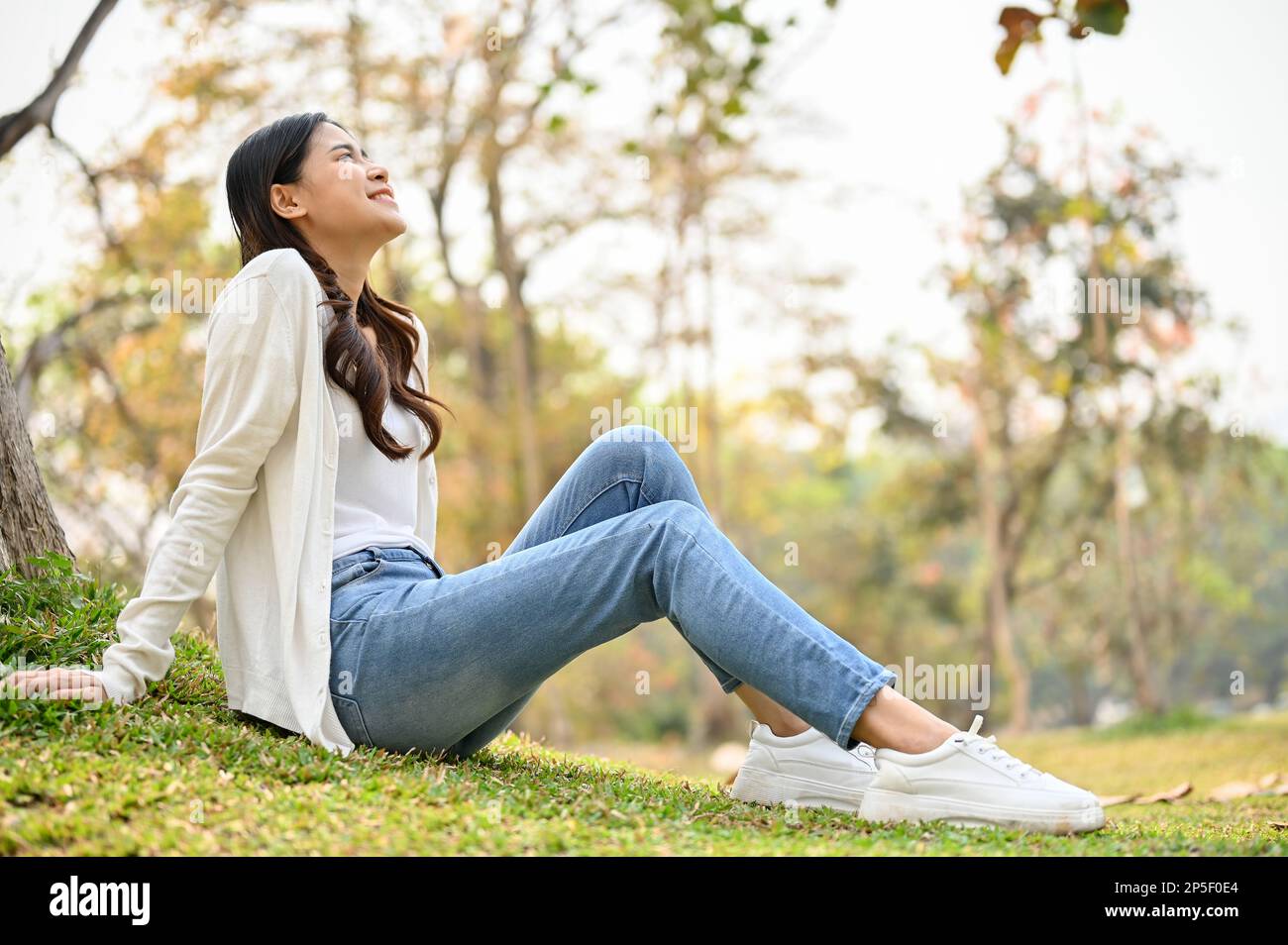 Carefree and happy young Asian woman in casual clothes sitting on grass ...