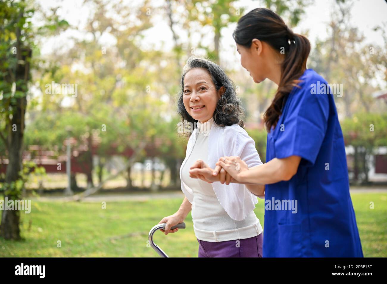 A happy old Asian disabled lady with a walking stick being helped by a ...