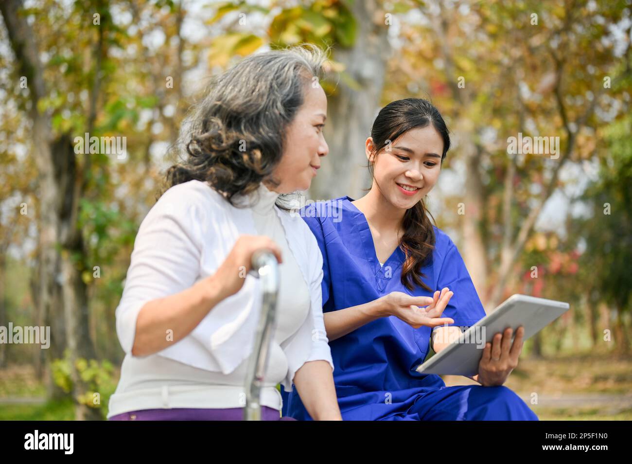 Happy and caring young Asian female nurse or caregiver shows something ...