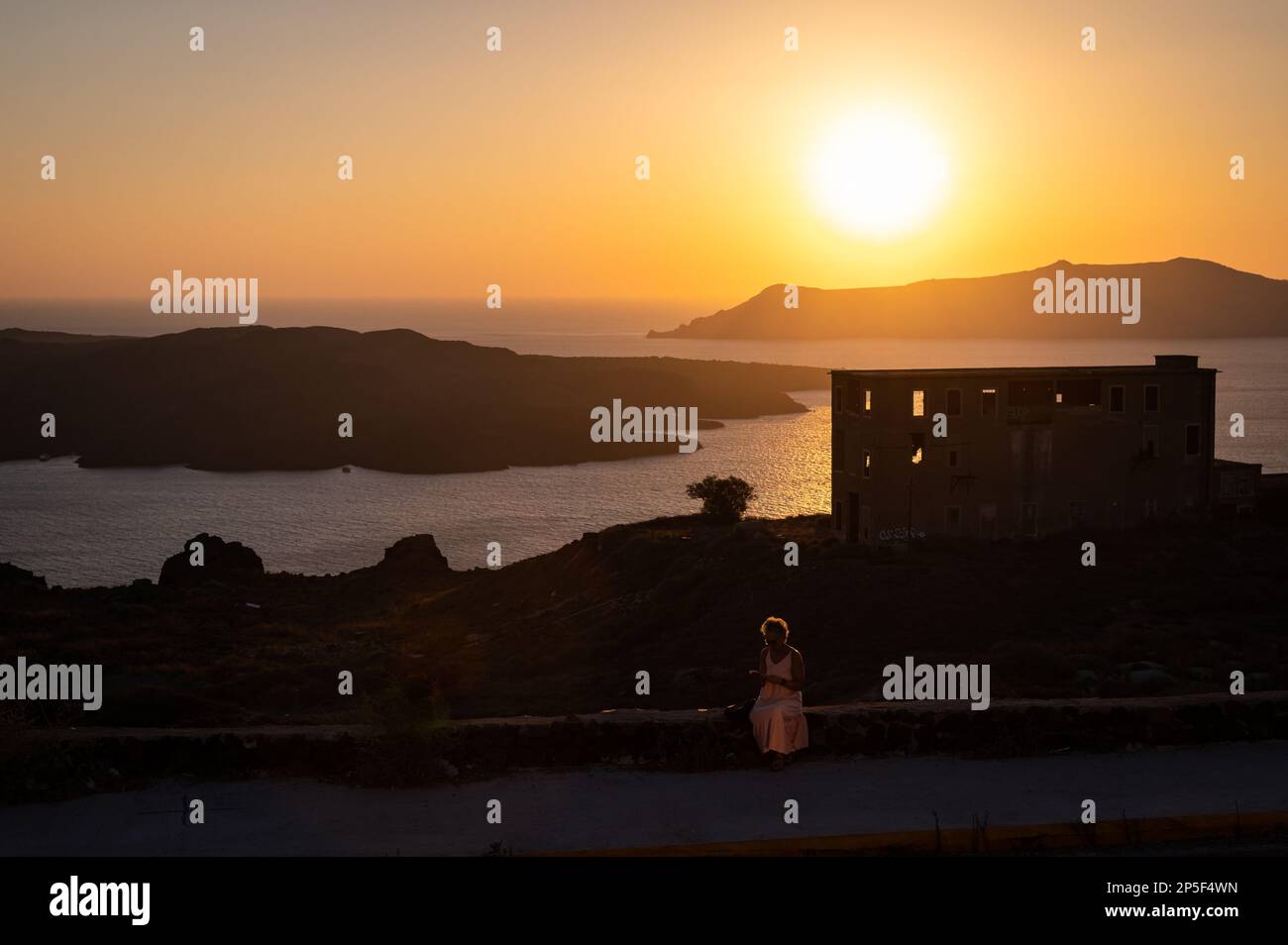Sunset view of Fira town on the Greek Island of Santorini. A woman sits ...