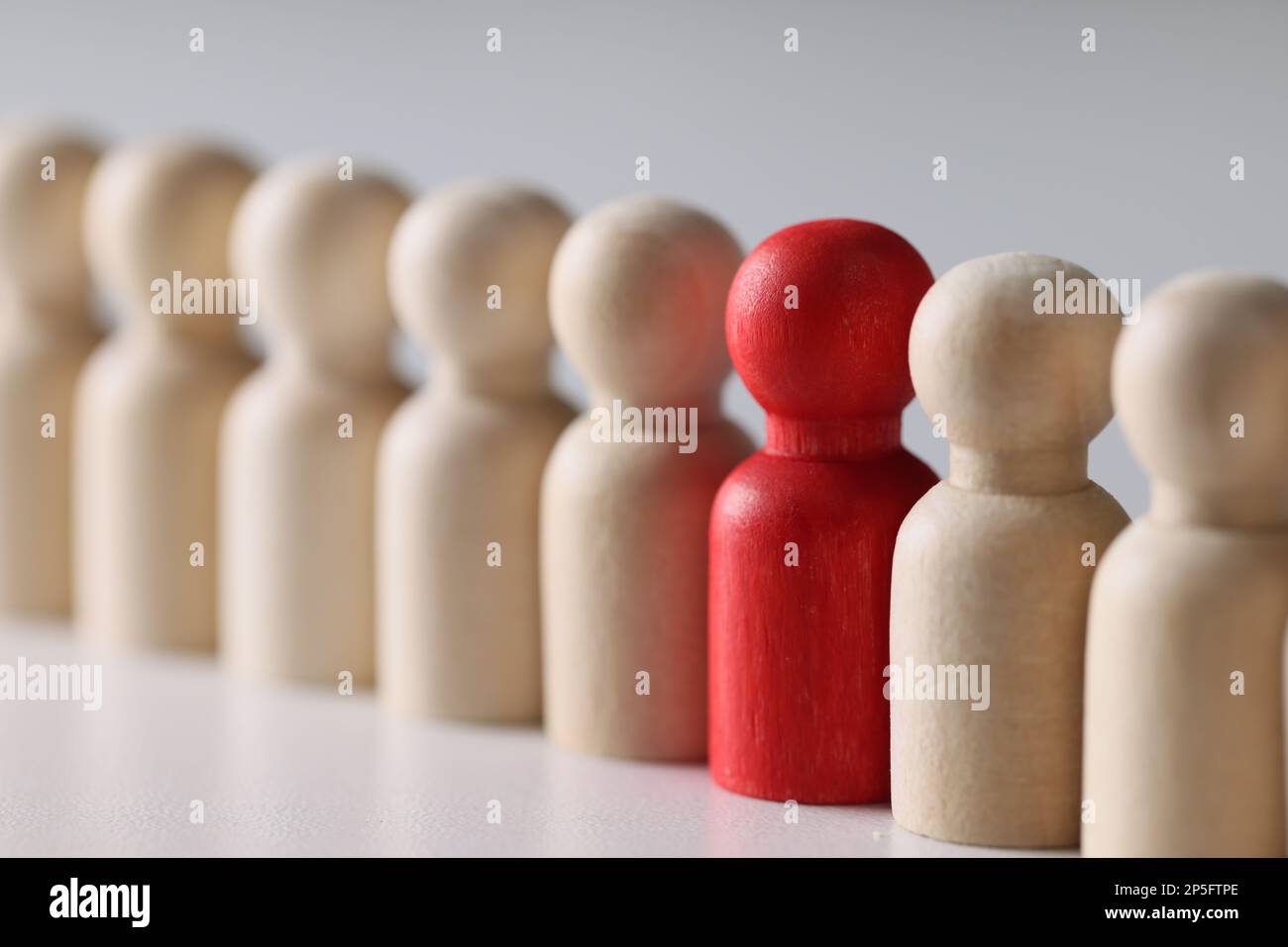 Red figure in row of many common wooden people figures Stock Photo - Alamy