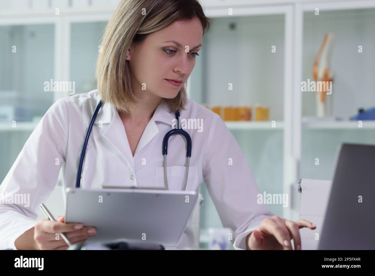 Female doctor holds clipboard with documents and works at computer in ...