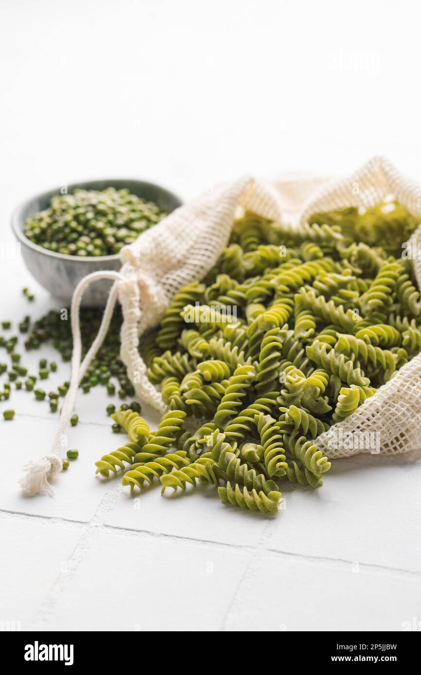 Green mung bean fusilli pasta on a white tile background. Bag with raw ...