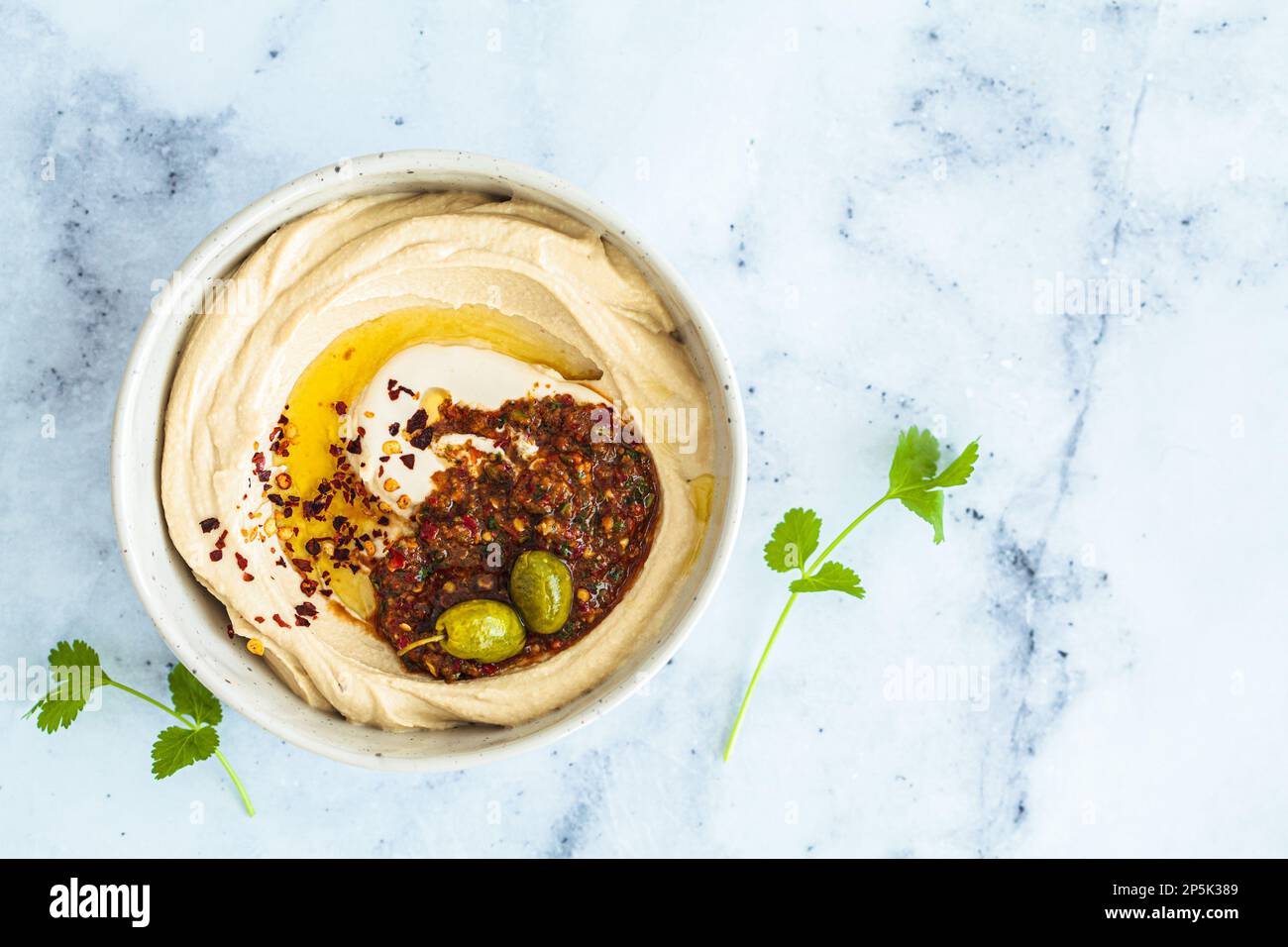 Homemade spicy hummus with tahini and olive oil in a bowl, white marble ...
