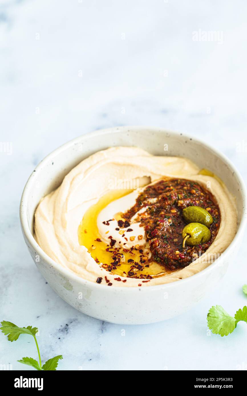 Homemade spicy hummus with tahini and olive oil in a bowl, white marble ...