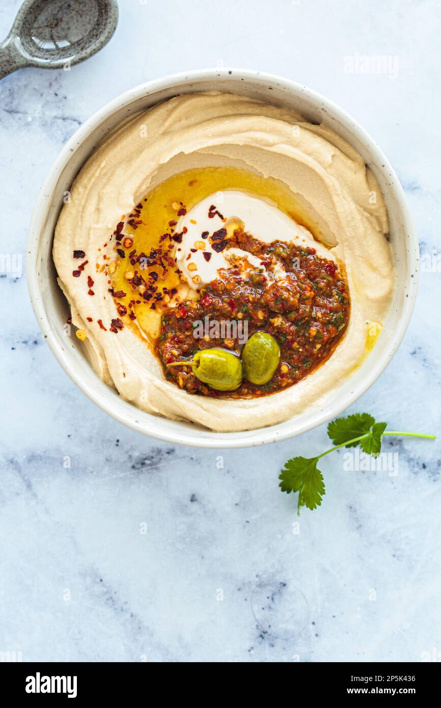 Homemade spicy hummus with tahini and olive oil in a bowl, white marble ...