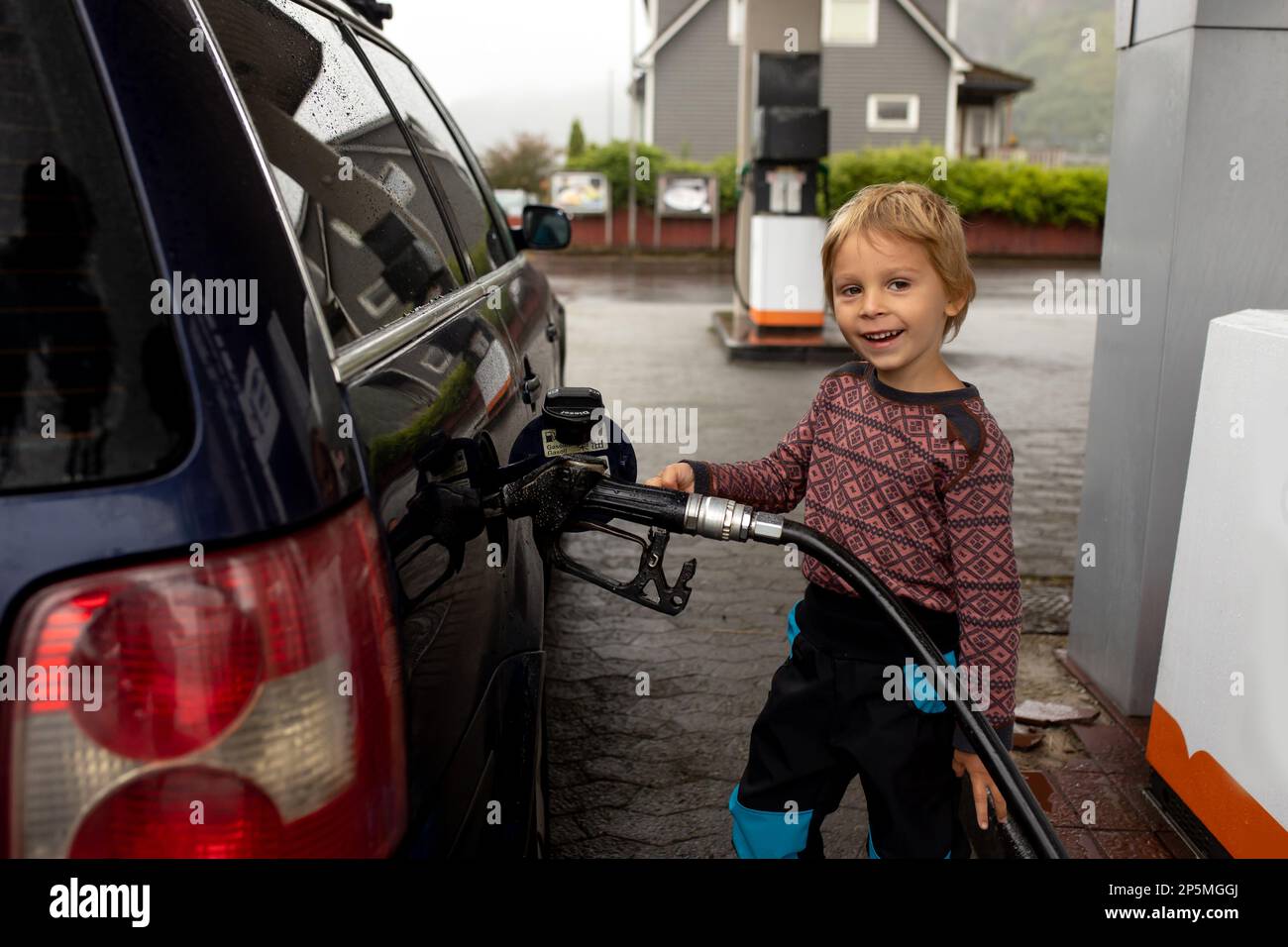 Sweet little child, blond boy, helping parents to put fuel in the car ...