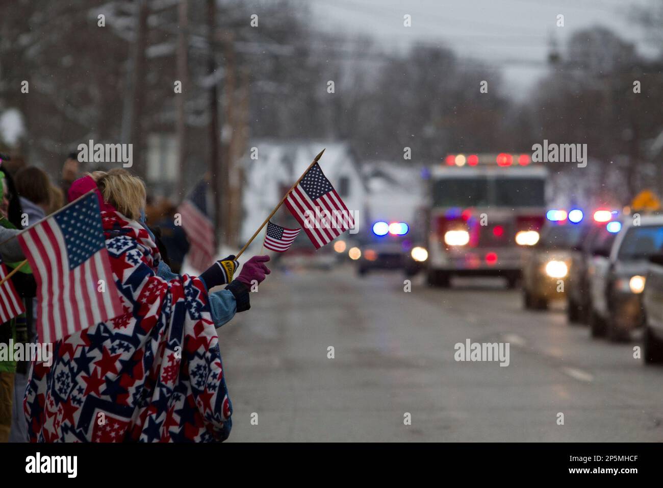 Onlookers wave flags as a procession of vehicles follows a hearse ...