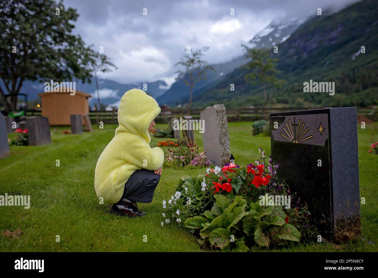Sad little child, blond boy, standing in the rain on cemetery, sad ...