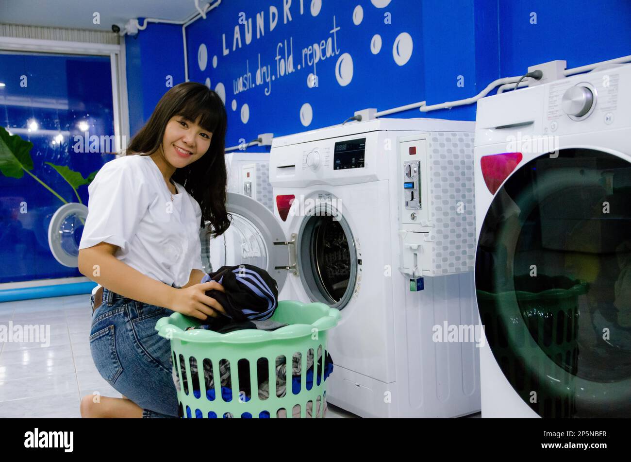Asian girl is washing cloths by washing machine in laundry shop with ...