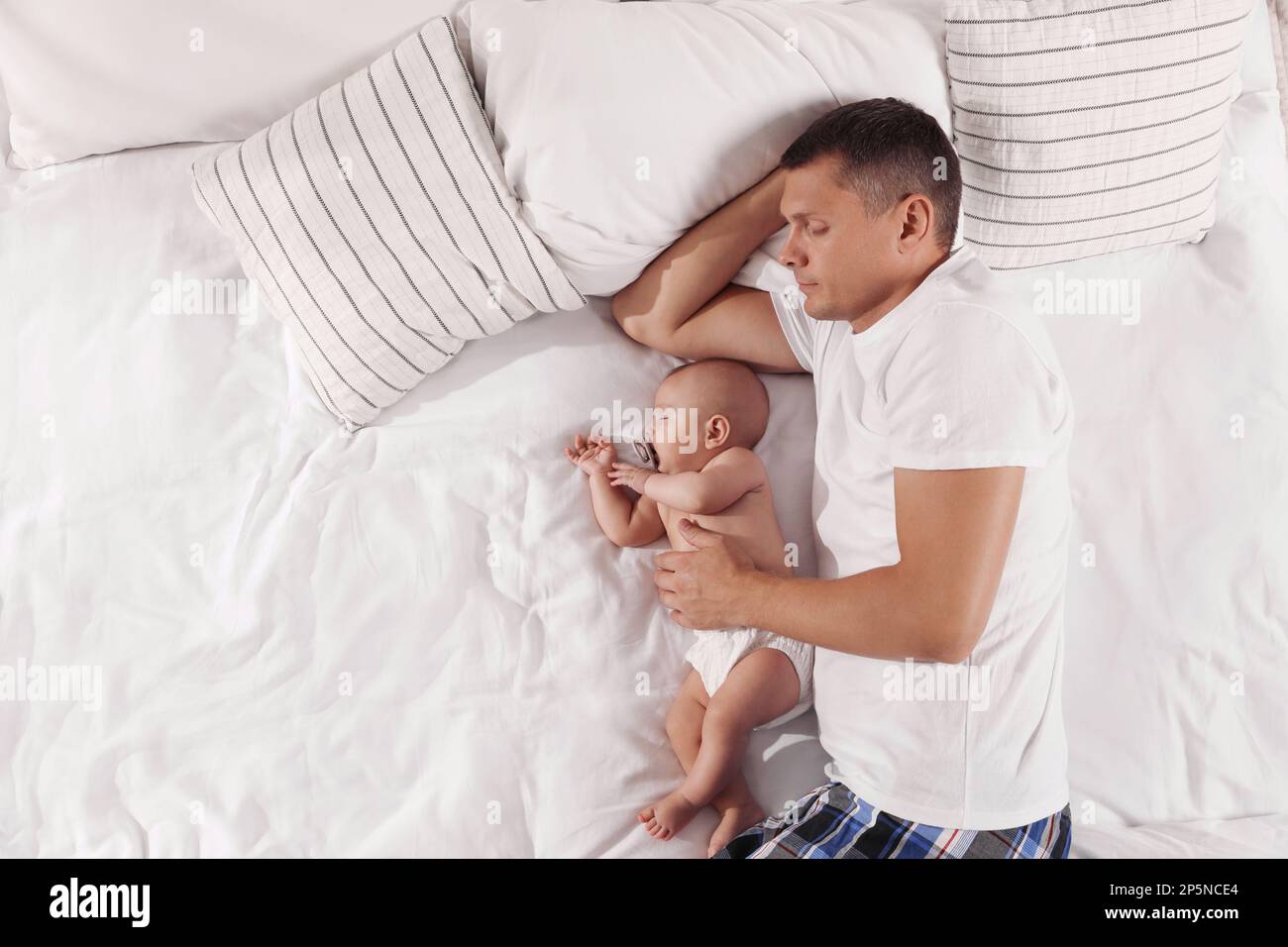 Father and baby sleeping on bed together, top view. Space for text ...