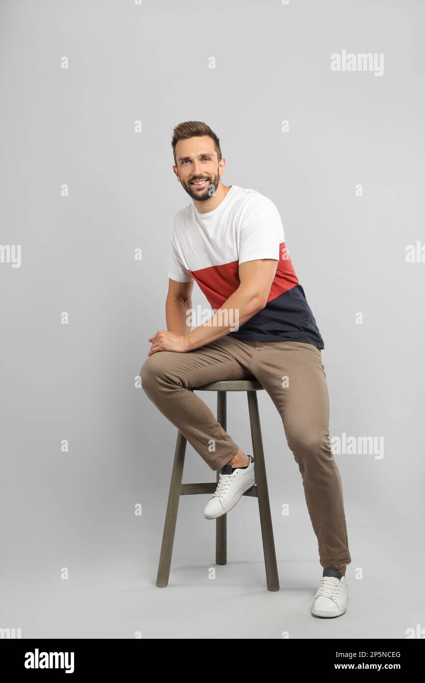 Handsome man sitting on stool against light grey background Stock Photo ...