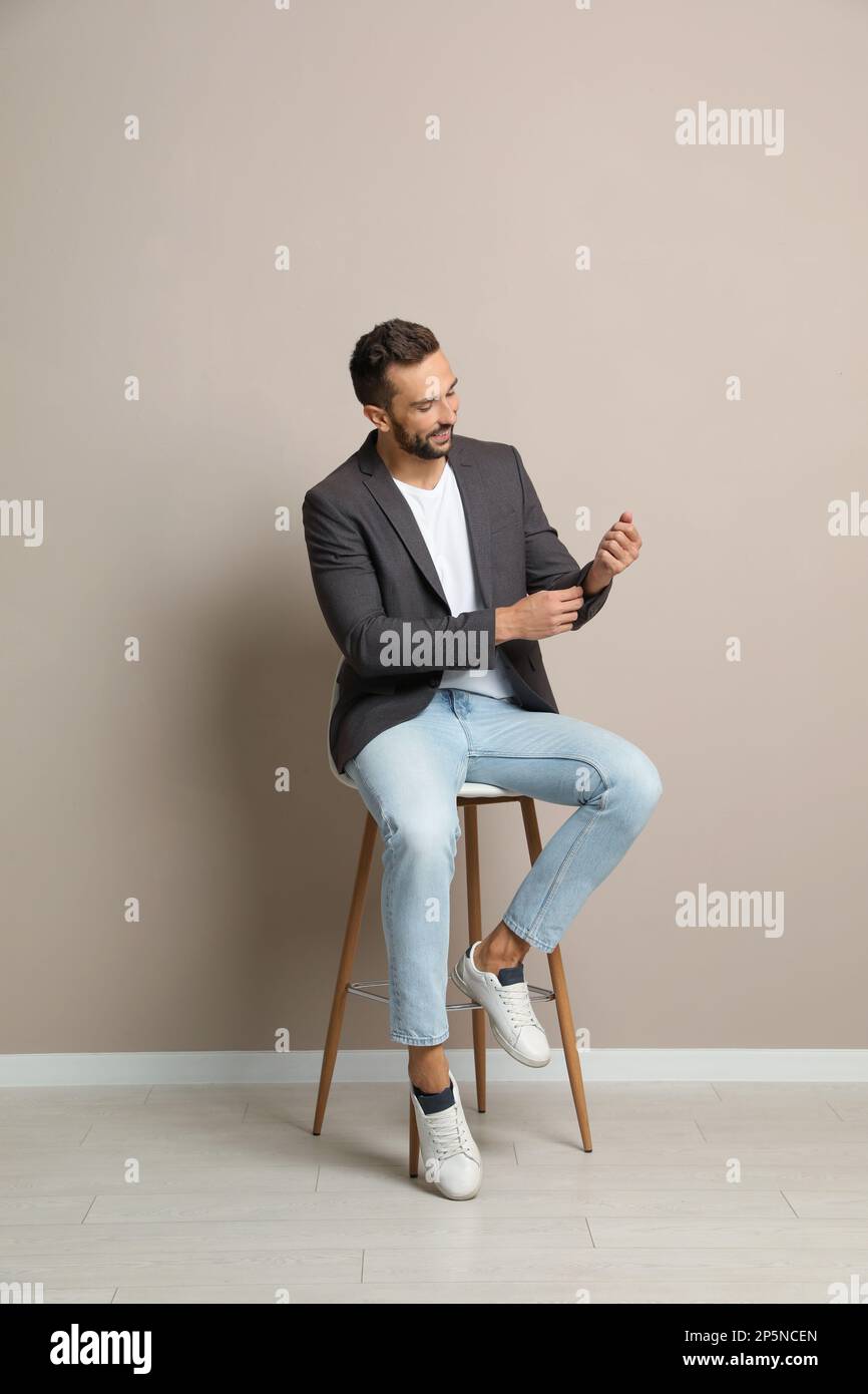 Handsome man sitting on stool near beige wall Stock Photo - Alamy