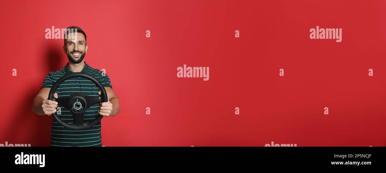 Happy man with steering wheel on red background Stock Photo - Alamy
