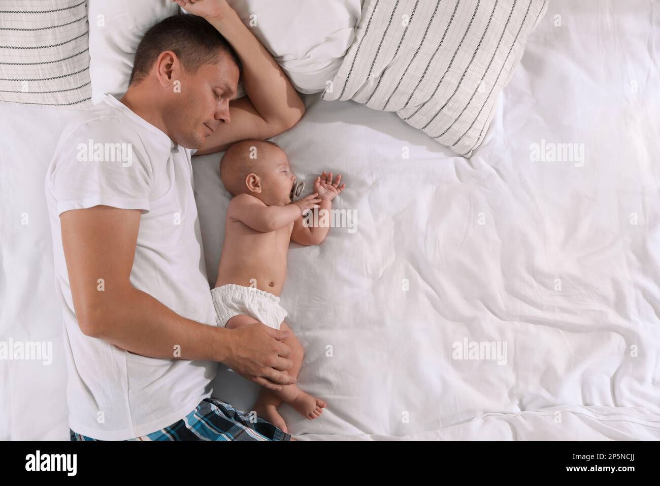 Father and baby sleeping on bed together, top view. Space for text ...