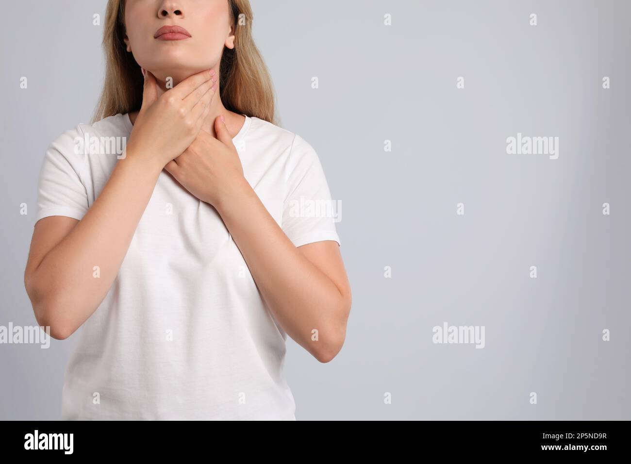 Young woman doing thyroid self examination on light grey background ...