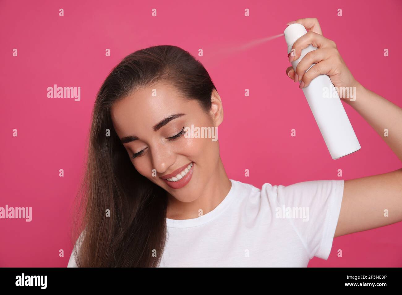 Young woman applying dry shampoo against pink background Stock Photo ...