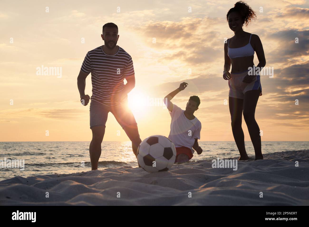 Friends playing football on beach at sunset Stock Photo - Alamy
