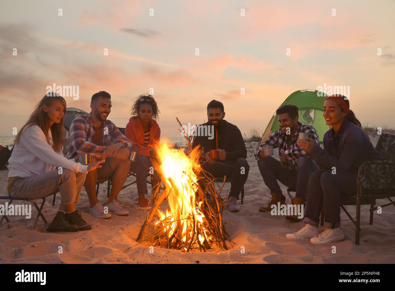 Friends sitting around bonfire on beach in evening Stock Photo - Alamy
