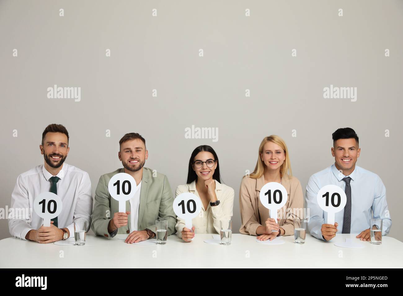 Panel of judges holding signs with highest score at table on beige ...
