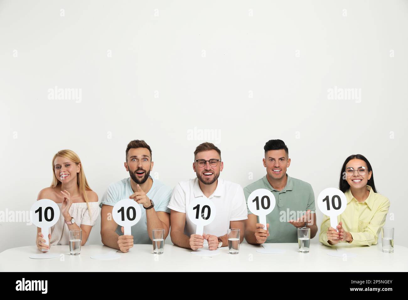 Panel of judges holding signs with highest score at table on white ...