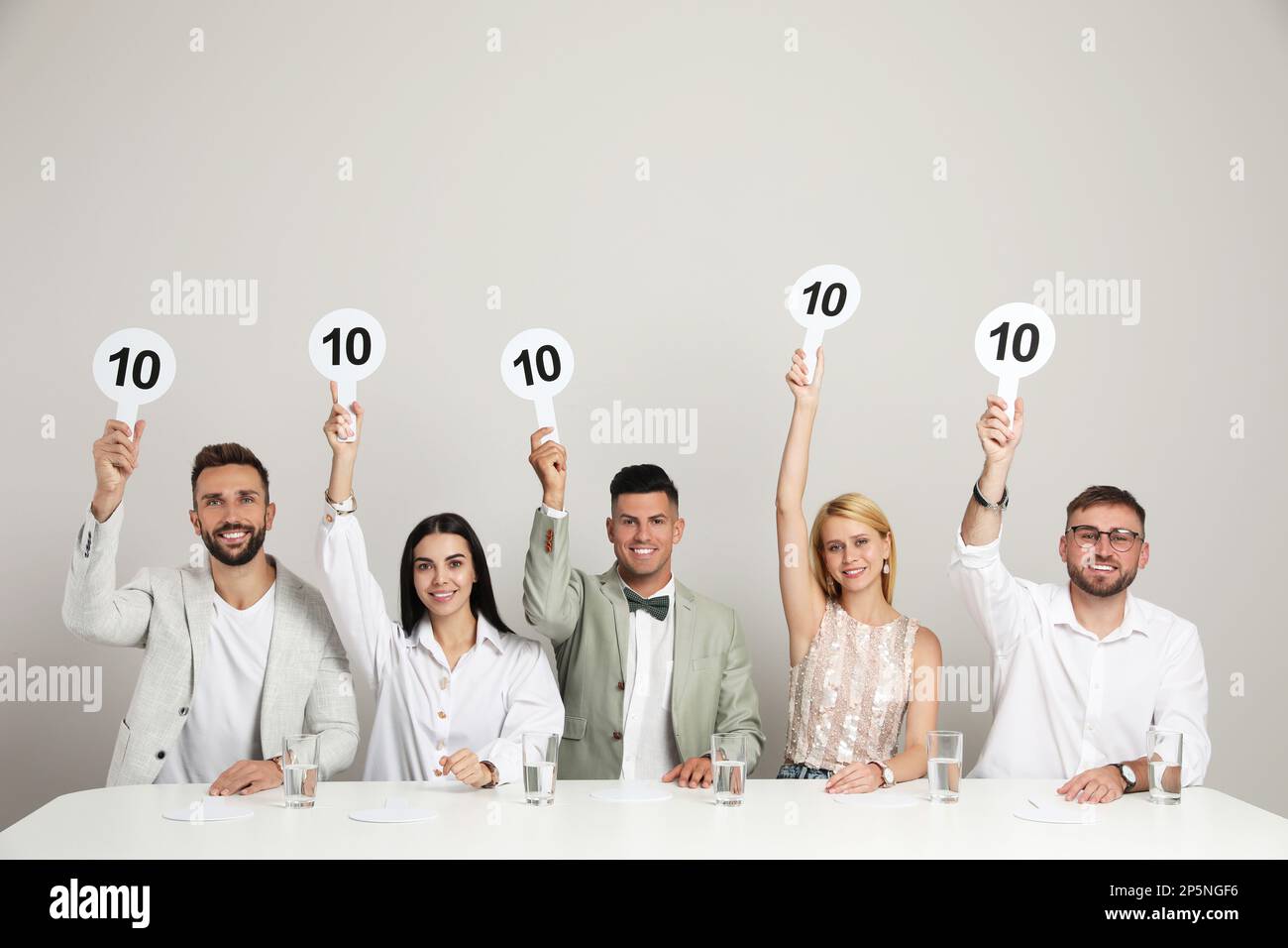 Panel of judges holding signs with highest score at table on beige ...
