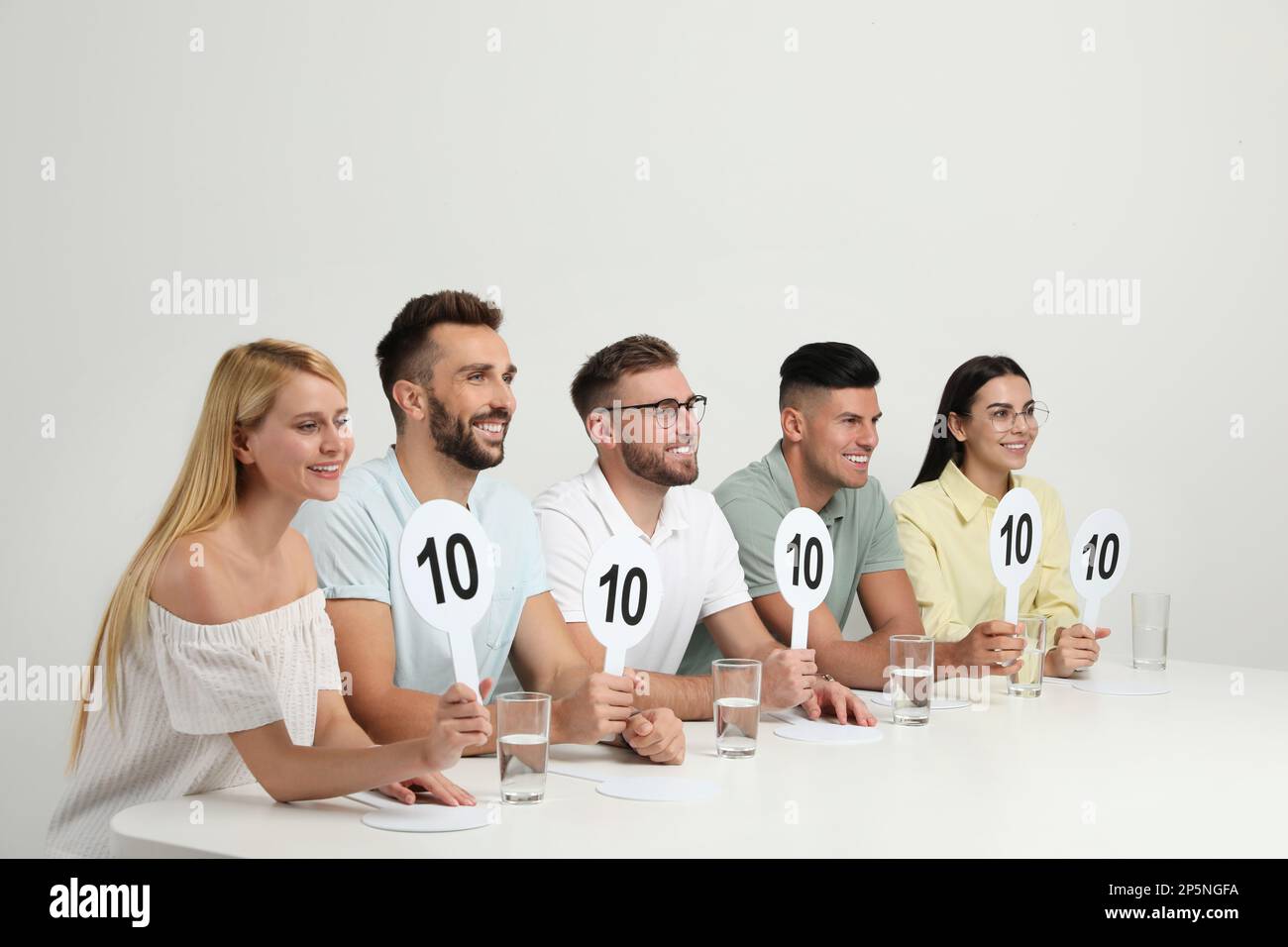 Panel of judges holding signs with highest score at table on white ...