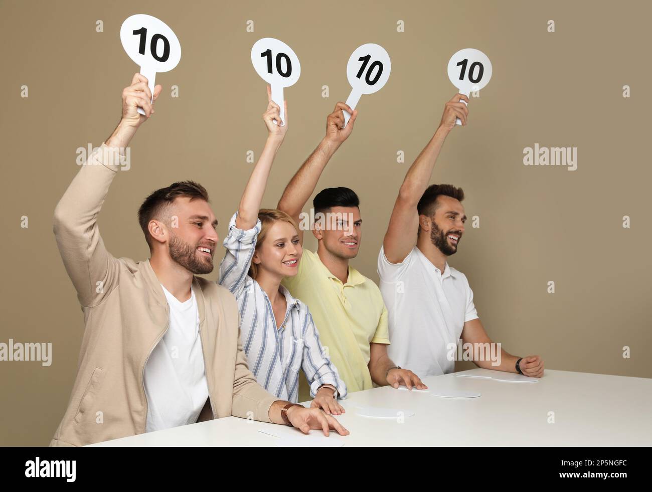 Panel of judges holding signs with highest score at table on beige ...