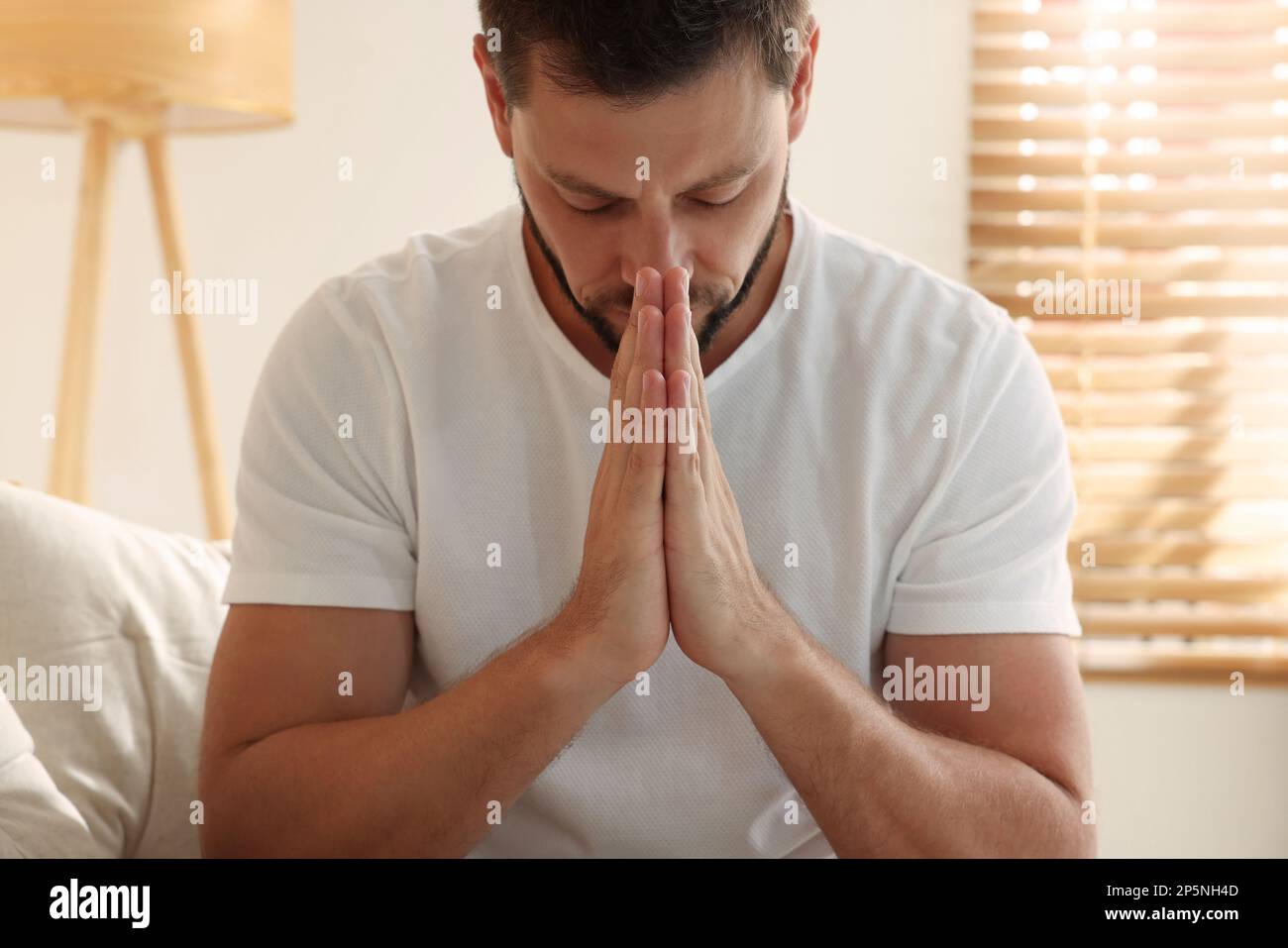 Religious man with clasped hands praying indoors Stock Photo - Alamy