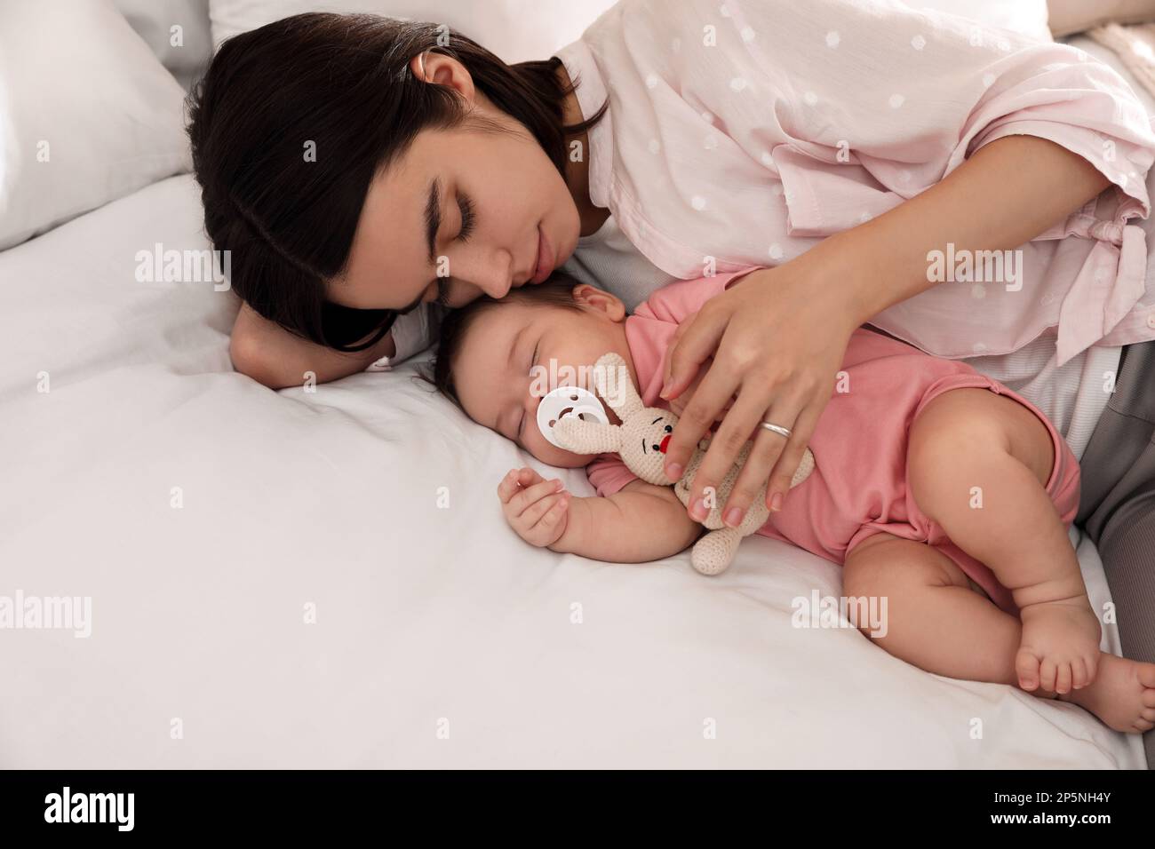 Young mother resting near her sleeping baby on bed. Space for text ...