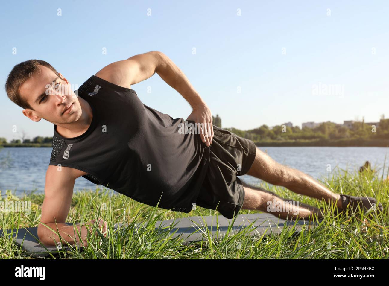 Sporty man doing side plank exercise on green grass near river Stock ...