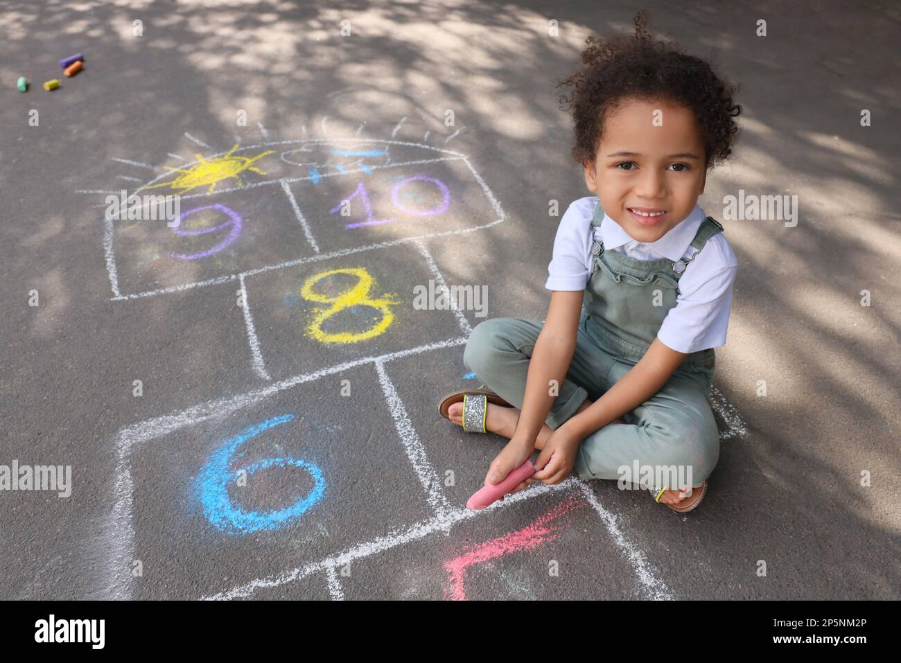Little African American girl drawing hopscotch with chalk on asphalt ...