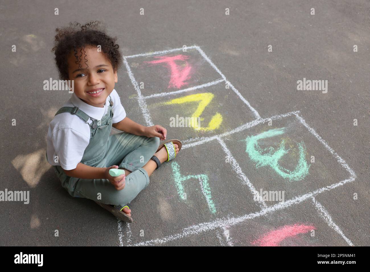 Little African American girl drawing hopscotch with chalk on asphalt ...
