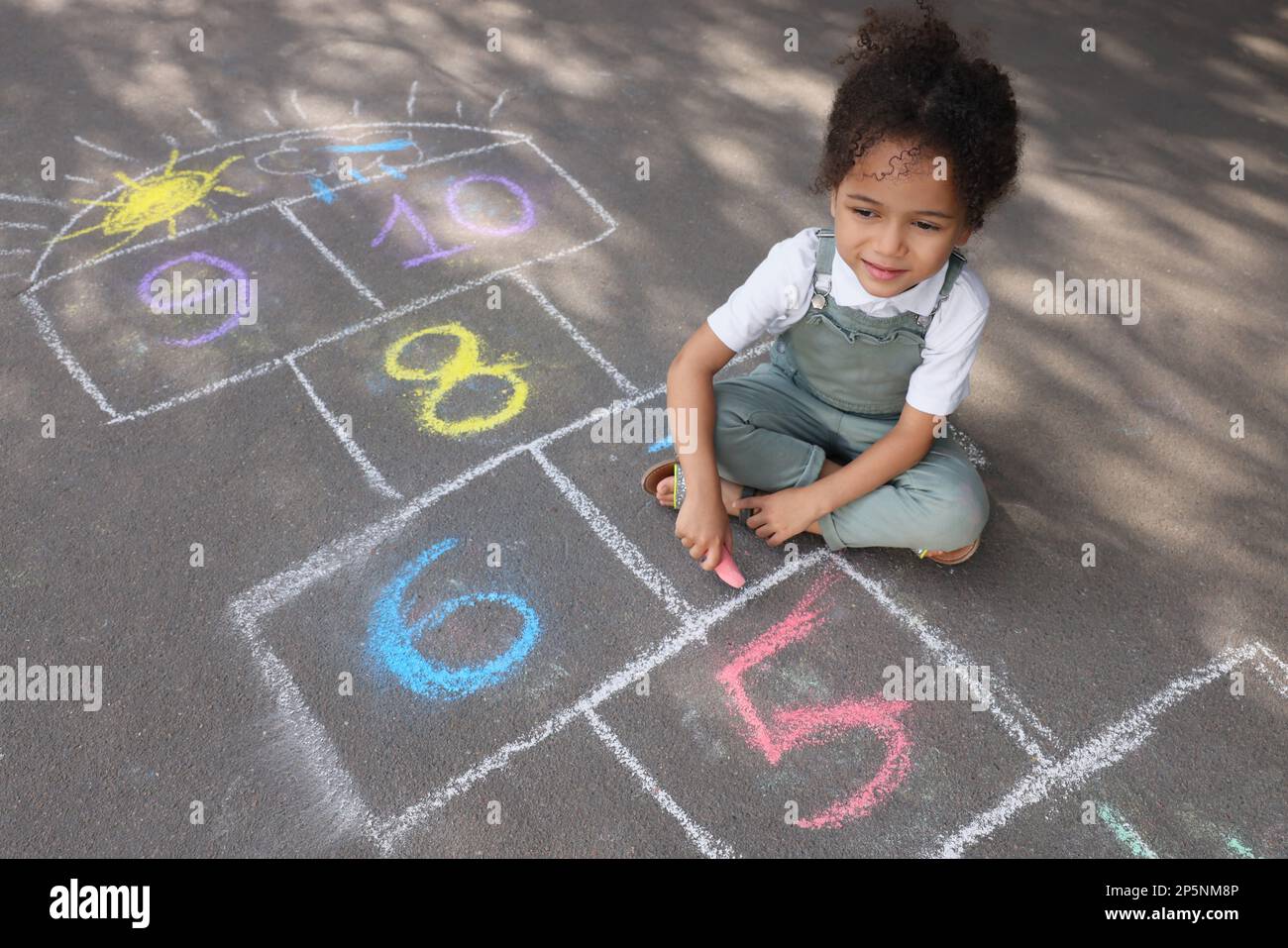 Little African American girl drawing hopscotch with chalk on asphalt ...