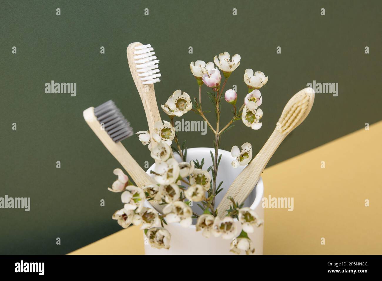 Wooden bamboo toothbrushes and flowers in a white glass on a green and ...