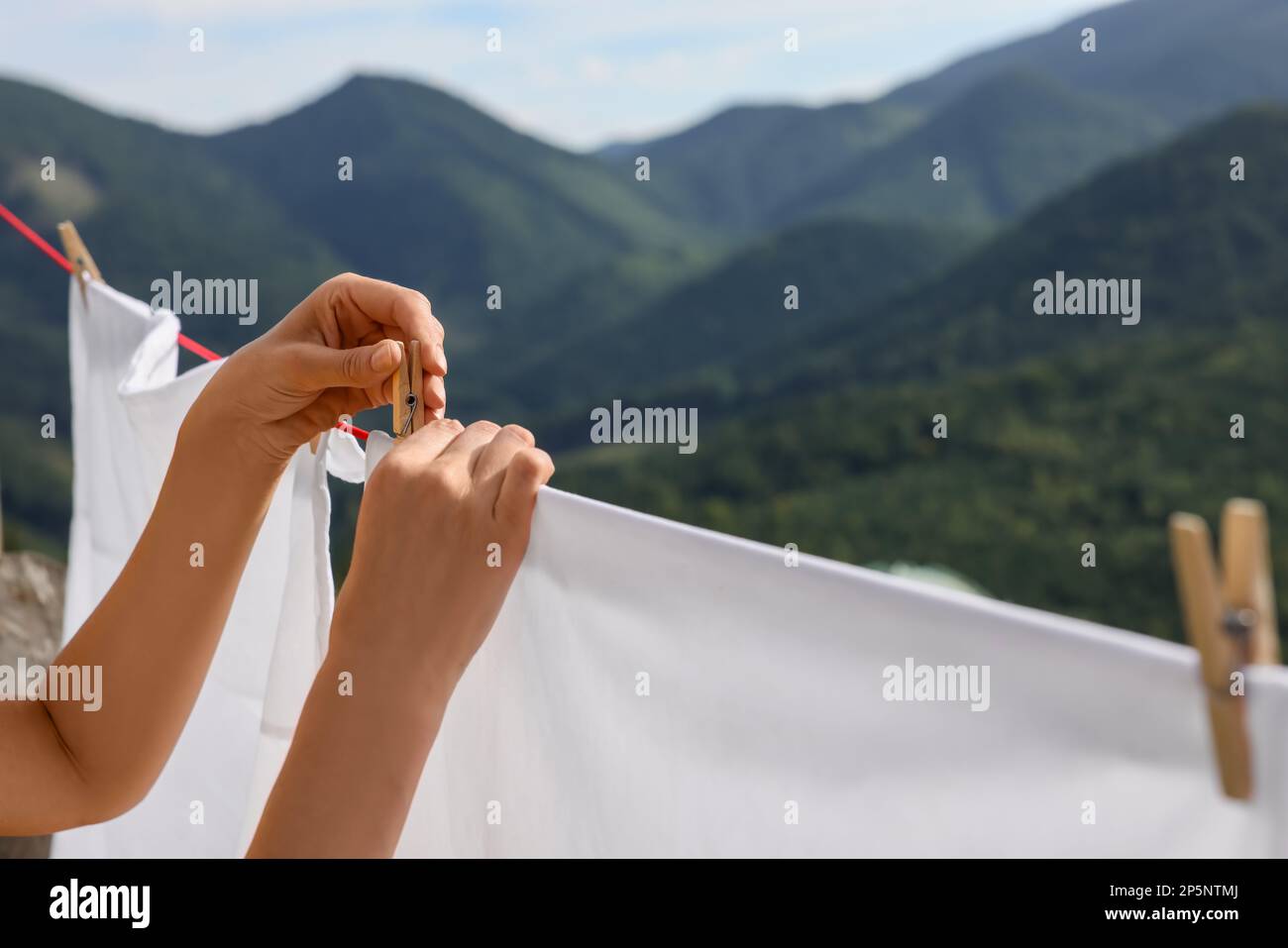 Woman hanging clean laundry with clothespins on washing line in ...