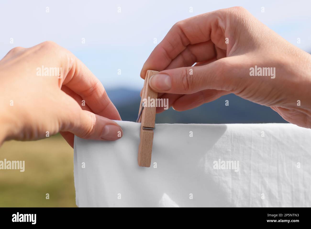 Woman hanging clean laundry with clothespin on washing line outdoors ...