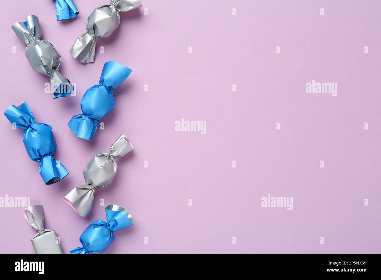 Many candies in light blue and silver wrappers on violet background ...