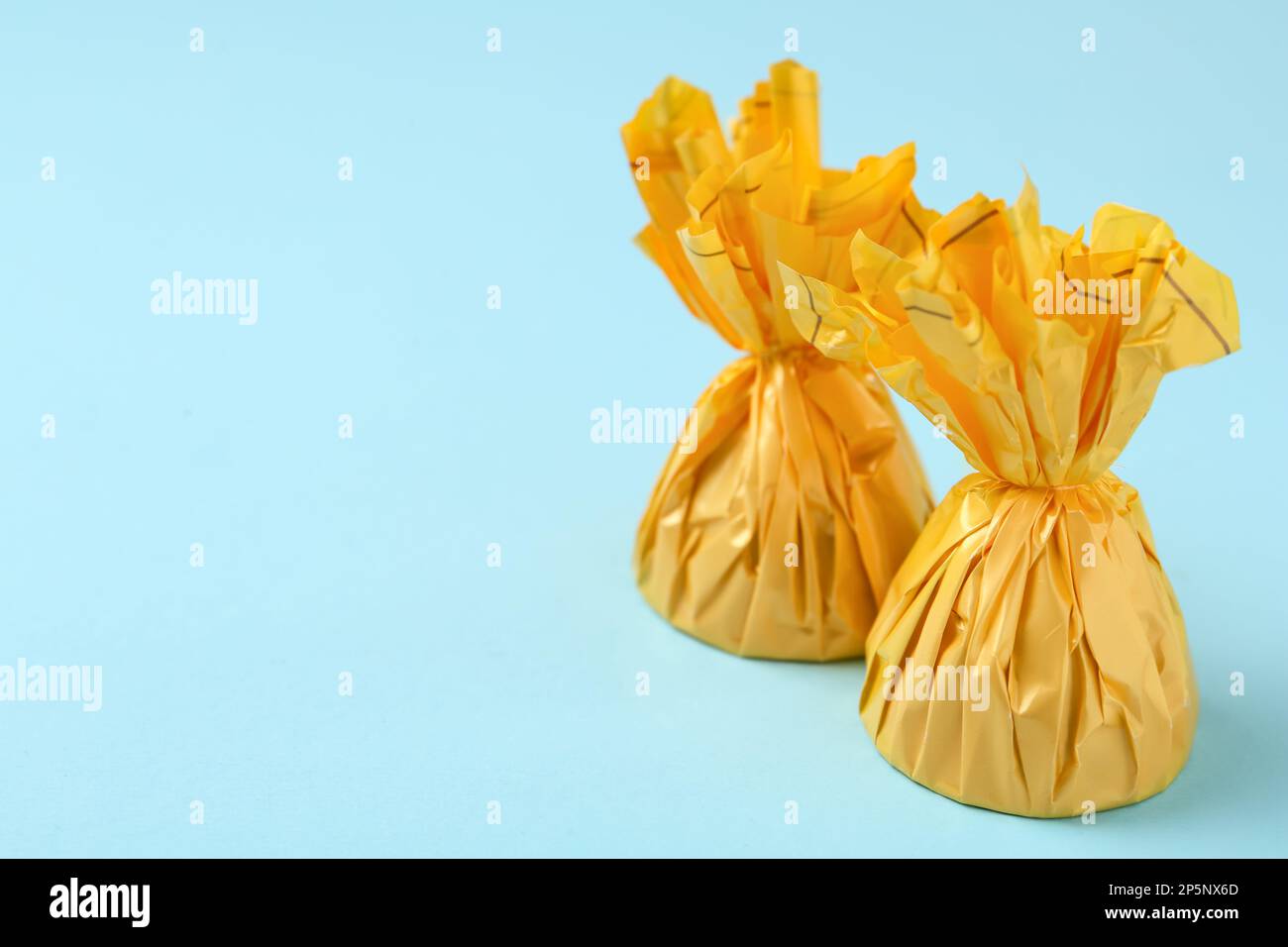 Candies in yellow wrappers on light blue background. Space for text ...