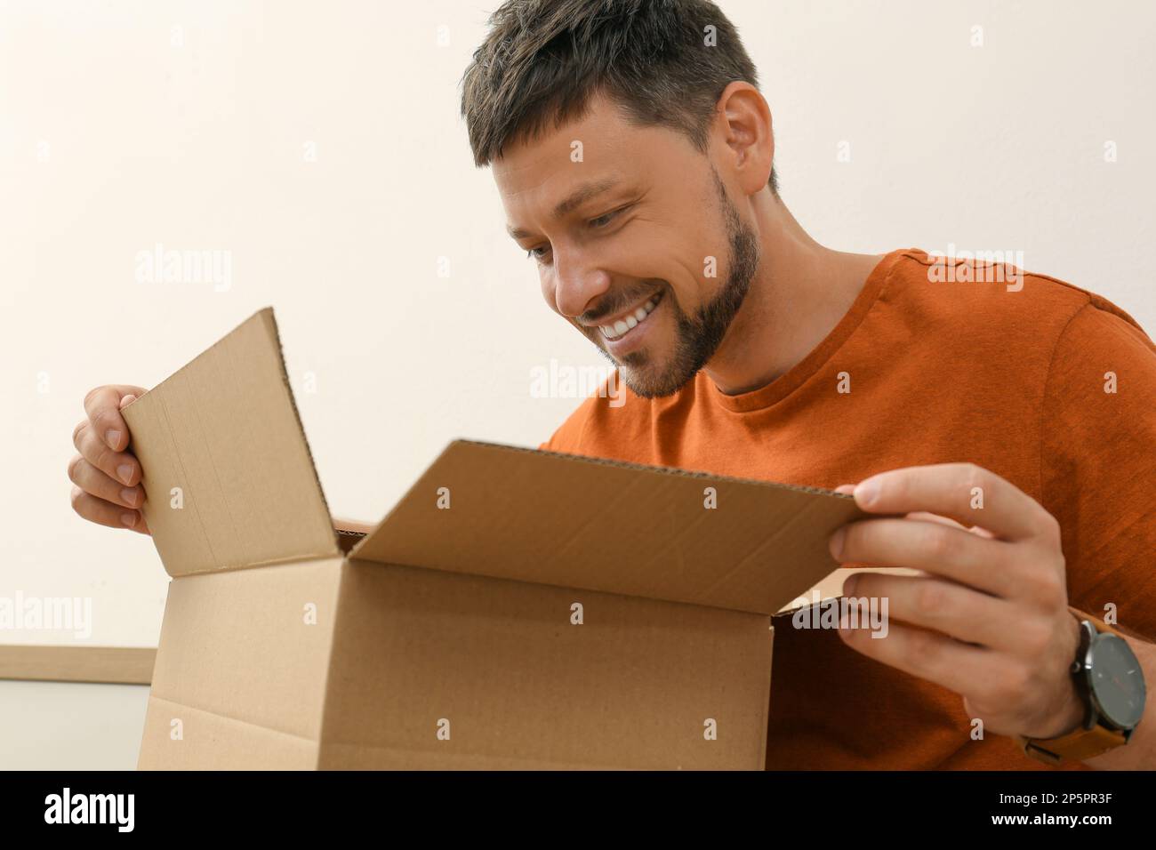 Happy man opening parcel indoors. Internet shopping Stock Photo - Alamy